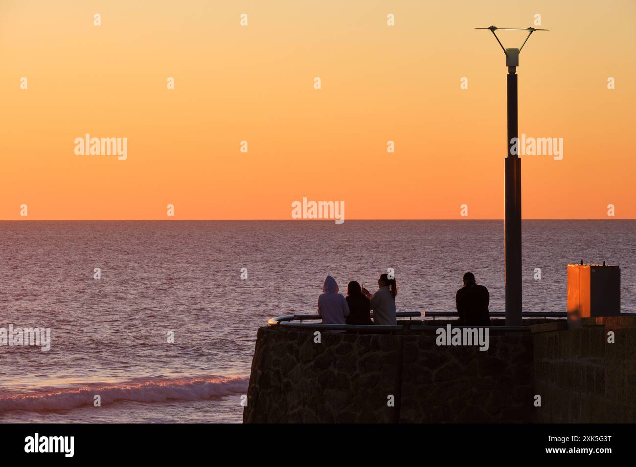 People watching the sunset in golden light from a beachside observation ...