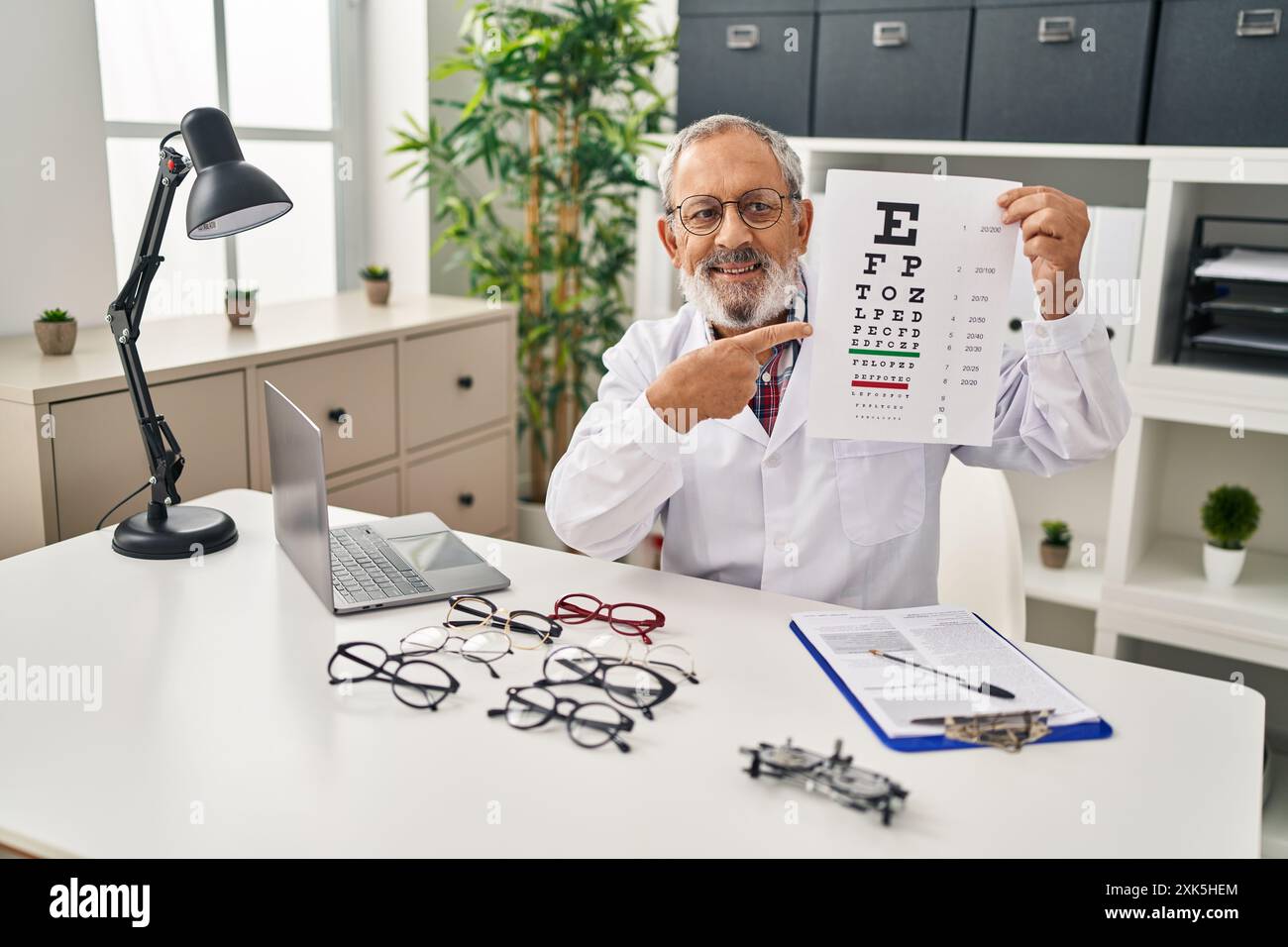 Cheerful senior man joyfully pointing at eye test chart at a clinic, a ...