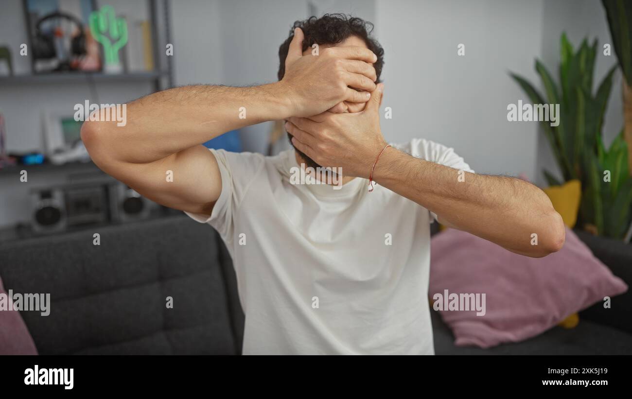 A distressed man covers his face with hands in a modern living room ...
