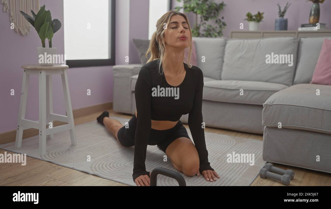A young woman in activewear practices yoga with closed eyes in a modern living room, exuding ...