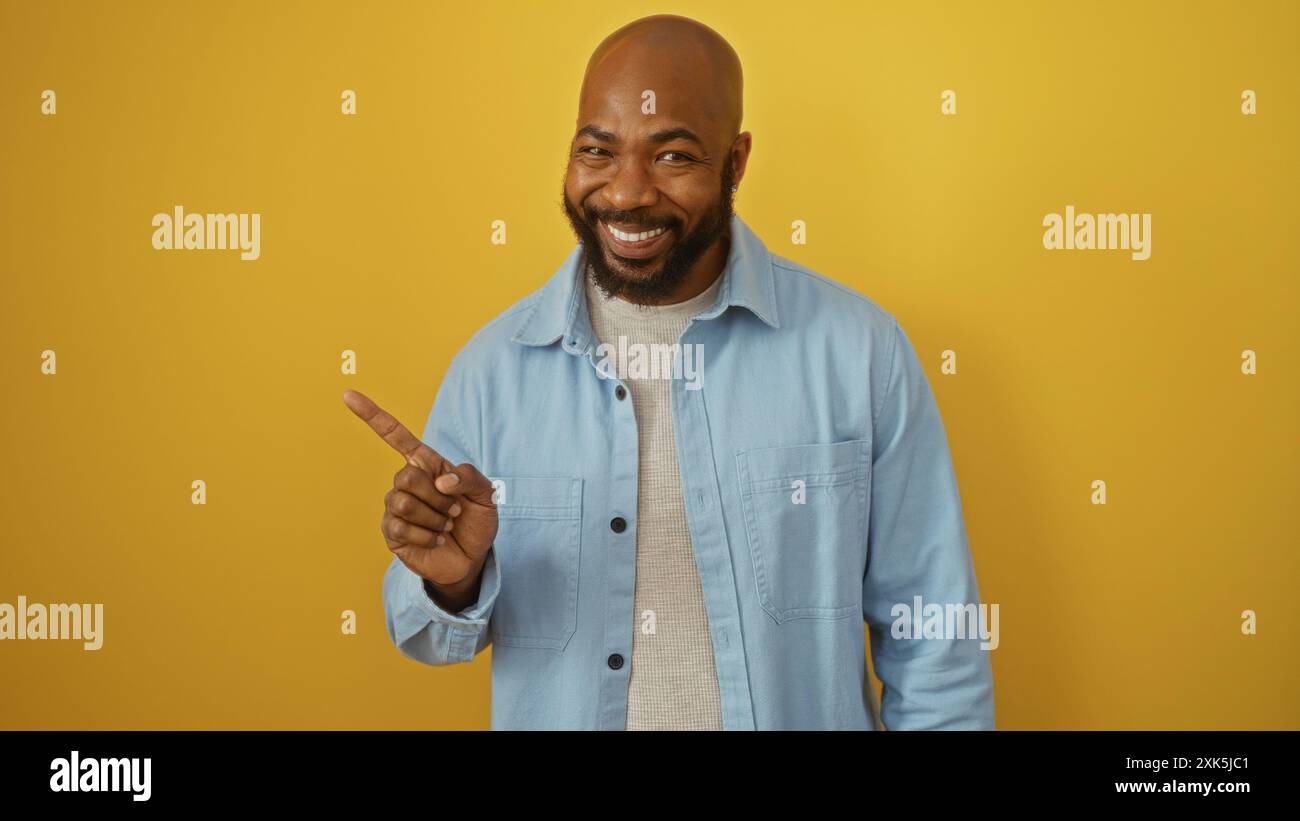 Handsome black man pointing against yellow background wall, wearing ...