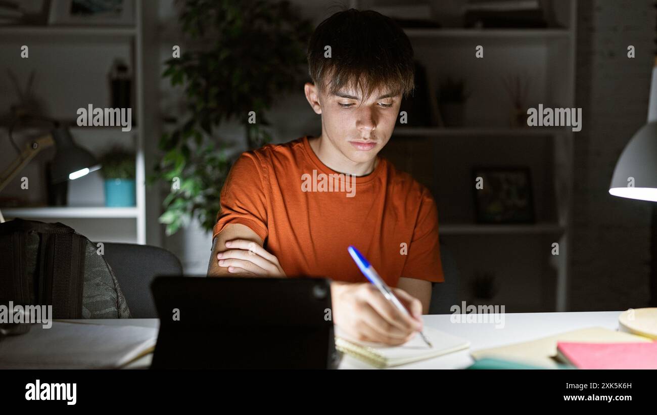 A concentrated young man studying late at night in a dimly lit home ...