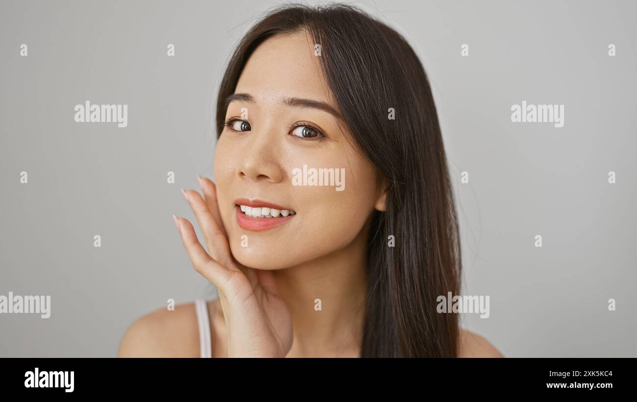 A beautiful young asian woman with a gentle smile poses against a white ...
