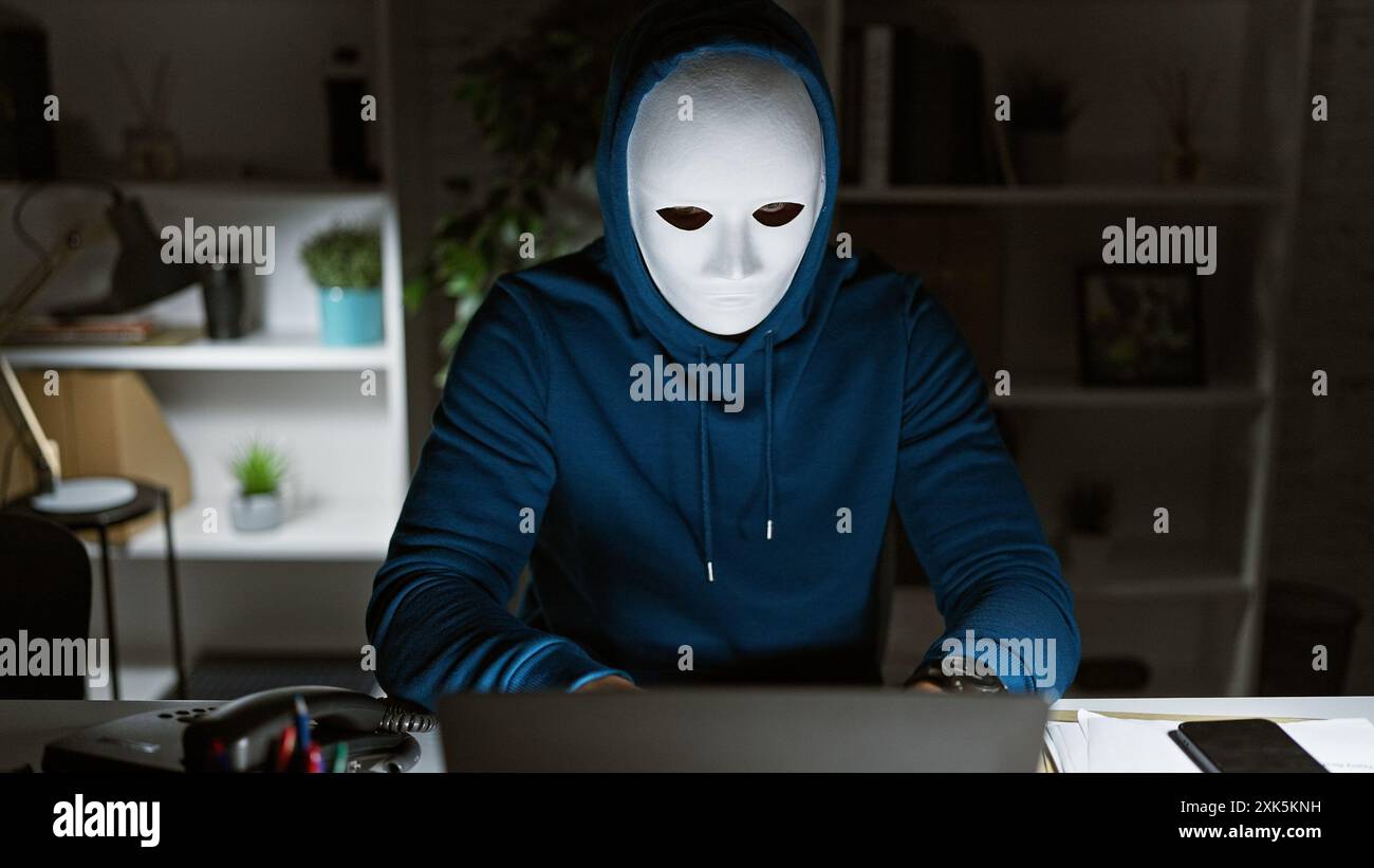 Mysterious person with a white mask and hoodie using computer in a dark ...