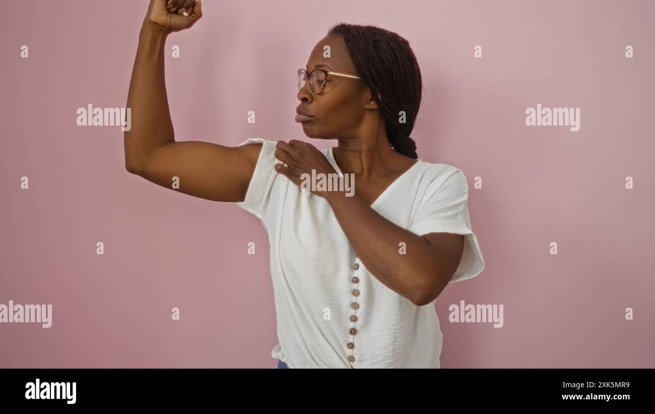 Confident woman flexing bicep in white shirt against pink background ...