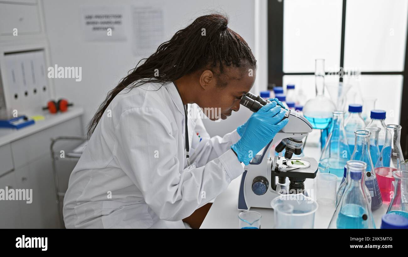 African woman scientist using microscope in laboratory with beakers ...