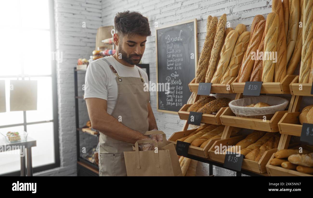 Young man with a beard and apron working in a bakery shop placing bread ...