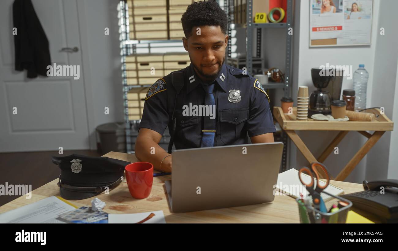 African american police officer focused on laptop in a well-equipped ...