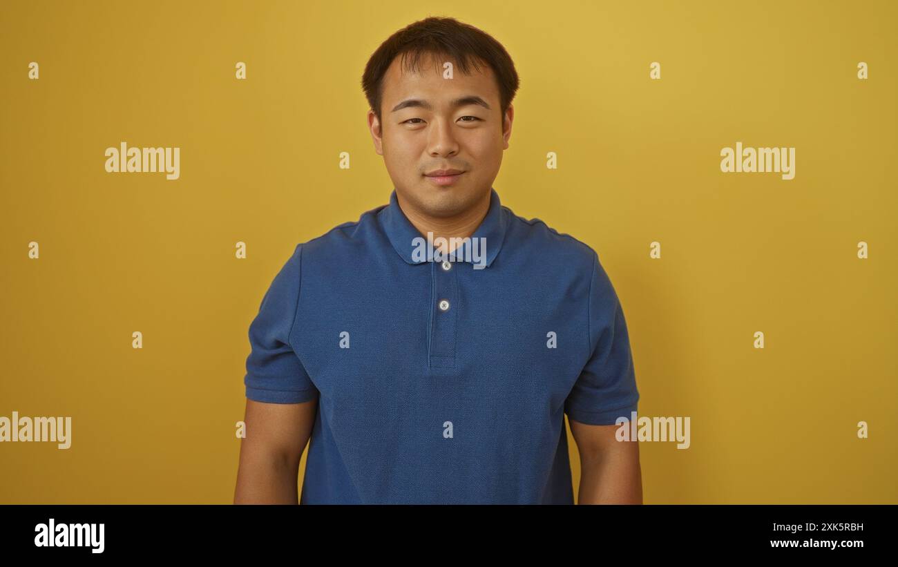 A handsome young chinese man stands against an isolated yellow wall ...