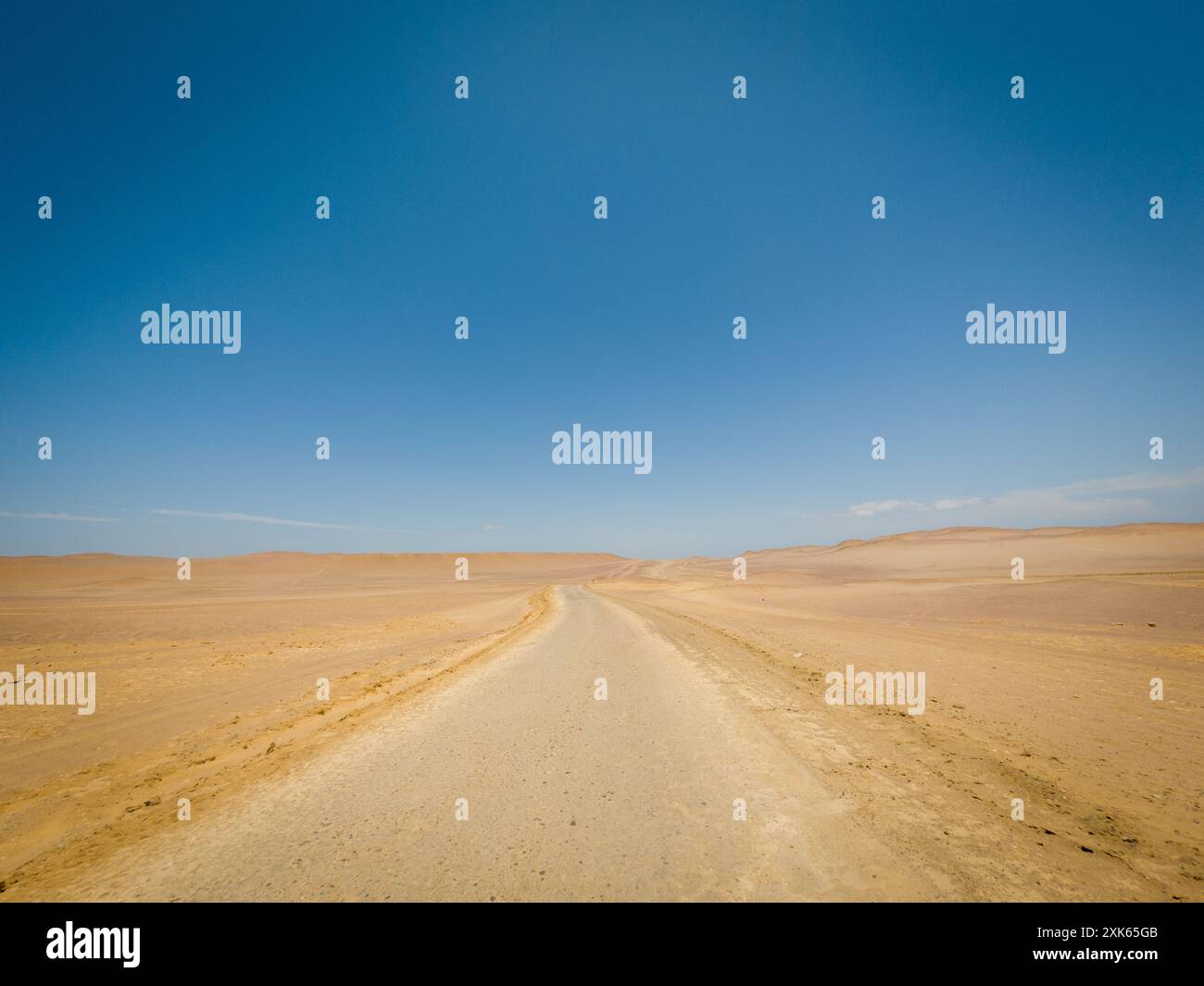 Desert road curving through sandy landscape under clear blue sky ...