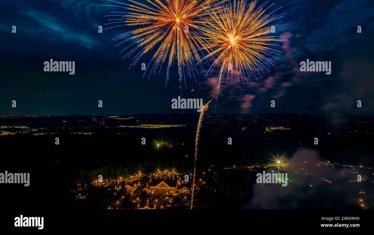 Golden And Blue Fireworks Burst Over A Lit Estate, Surrounded By Trees ...