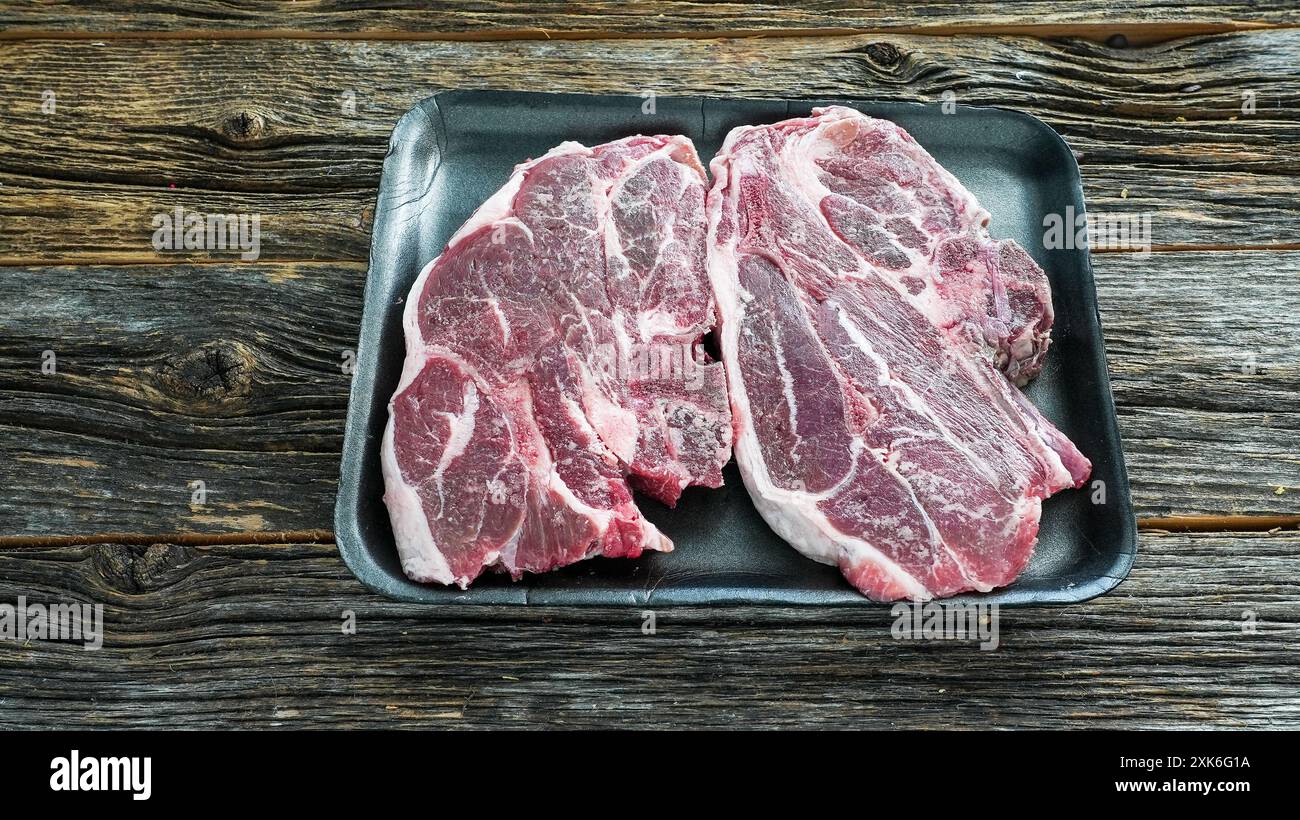 Two raw lamb shoulder chops are in a black styrofoam tray against a ...