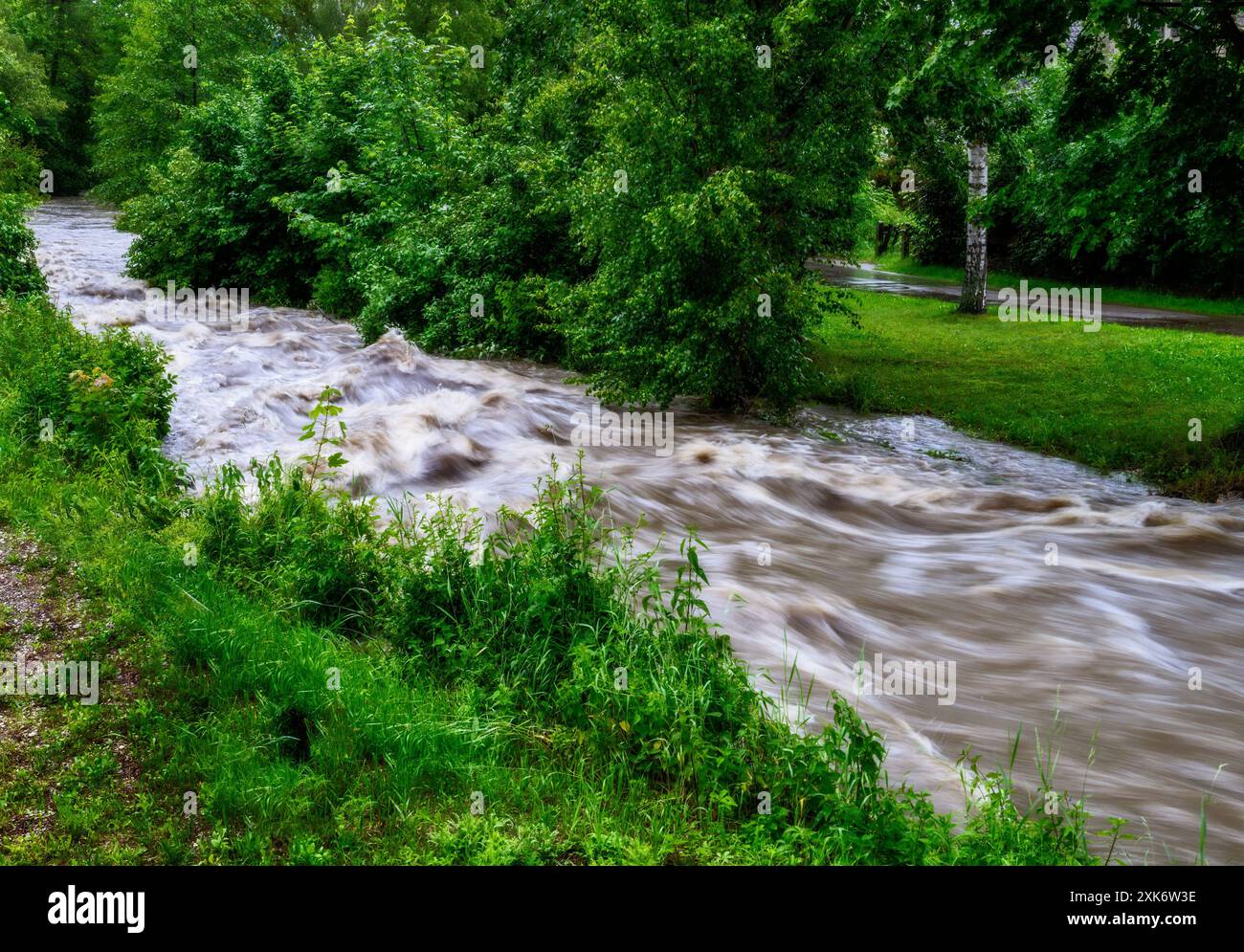 Fast flowing river after heavy rain and a partially flooded street ...