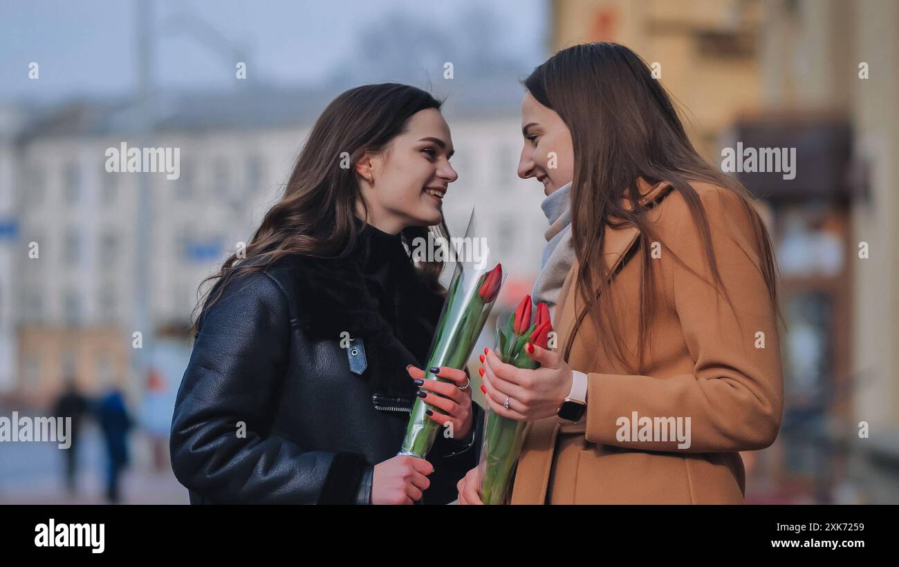 two happy girls, students, friends with flowers in their hands ...