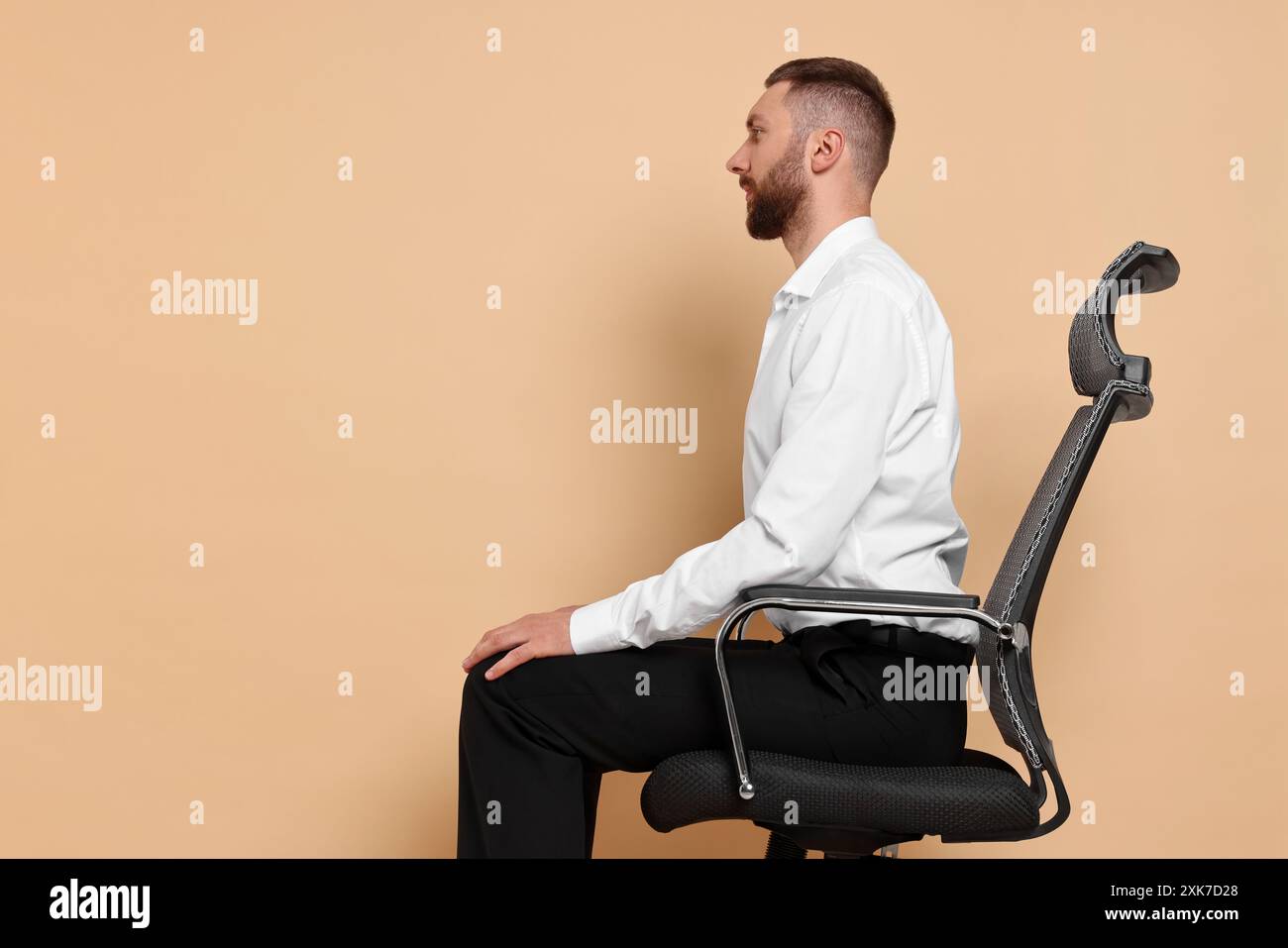 Man with good posture sitting on chair against pale orange background ...