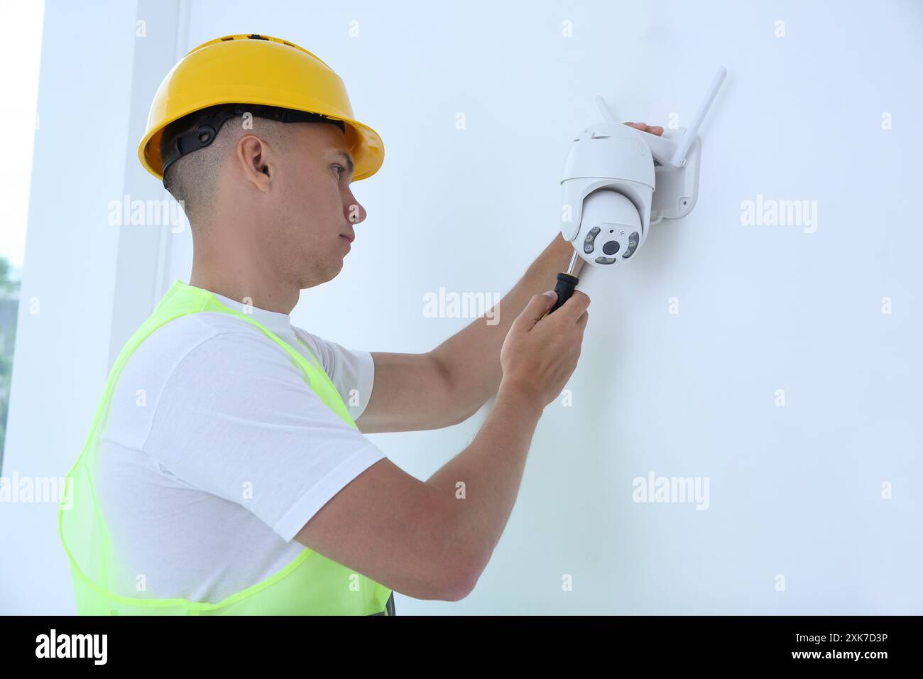 Technician with screwdriver installing CCTV camera on wall indoors ...