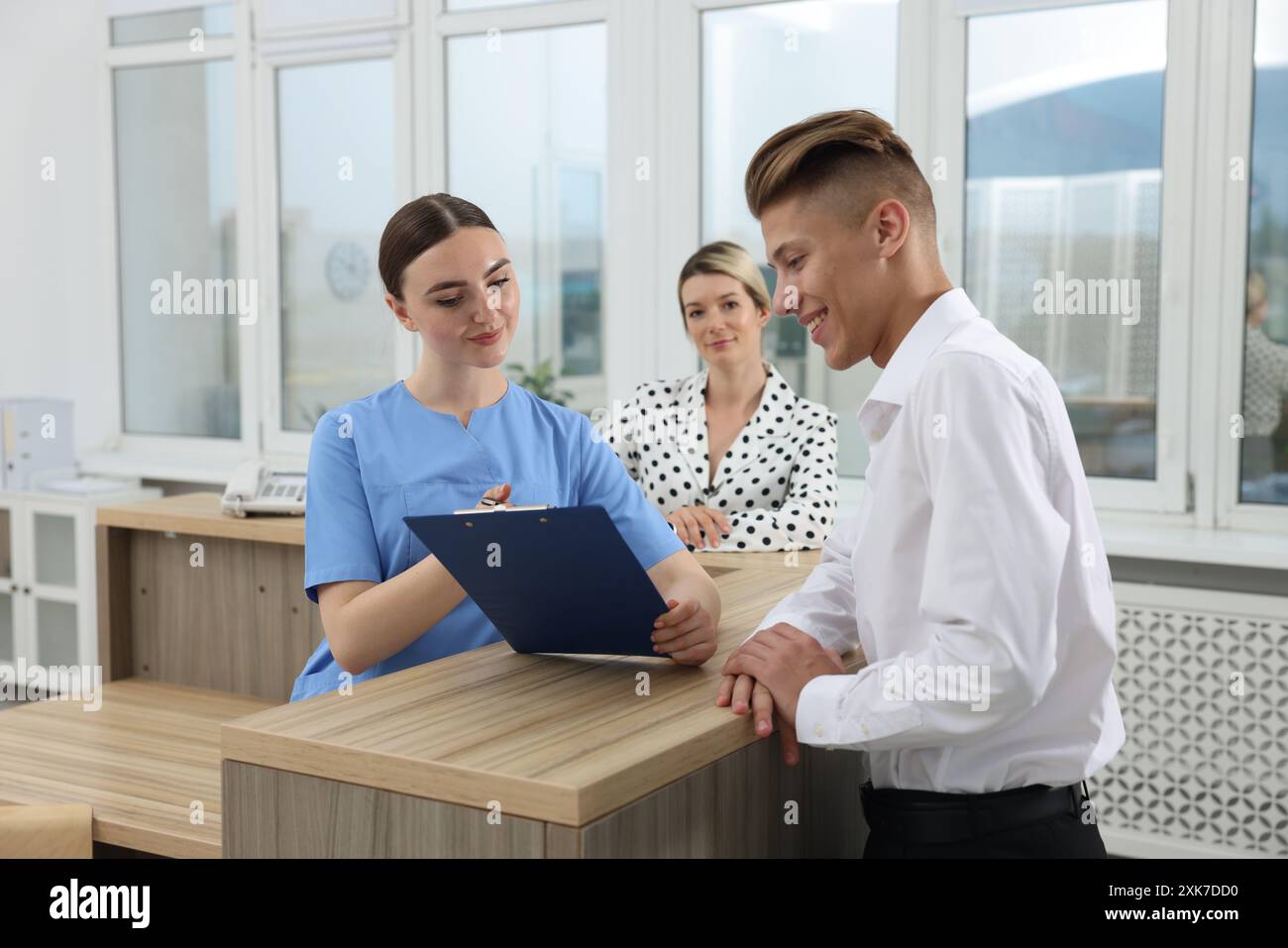 Professional receptionist working with patients at wooden desk in ...