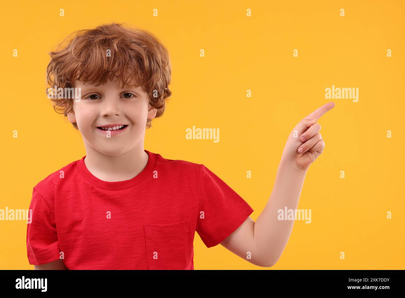 Portrait of cute little boy pointing at something on orange background ...