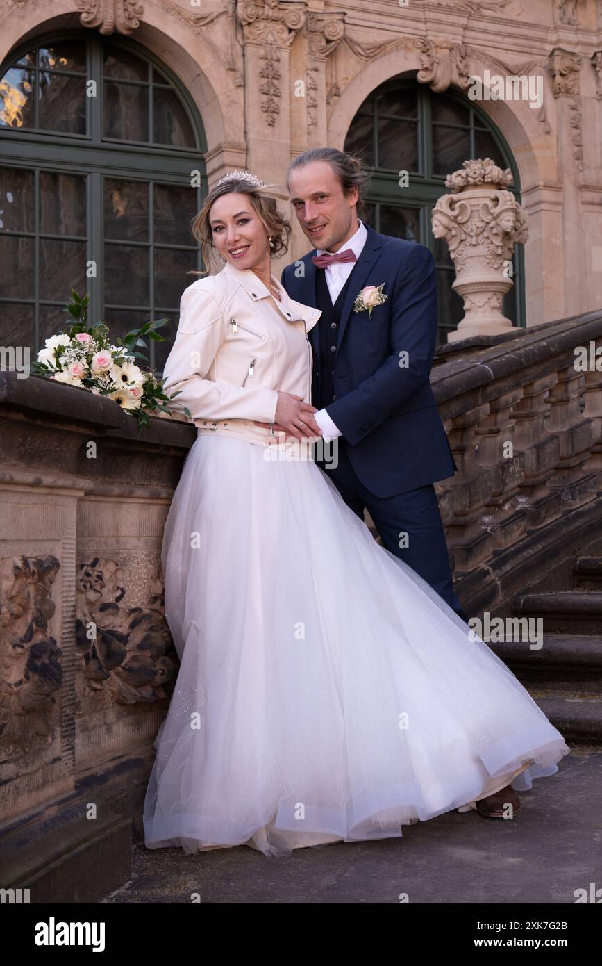 A cute bride in a dress with a train and groom posing on steps of a ...
