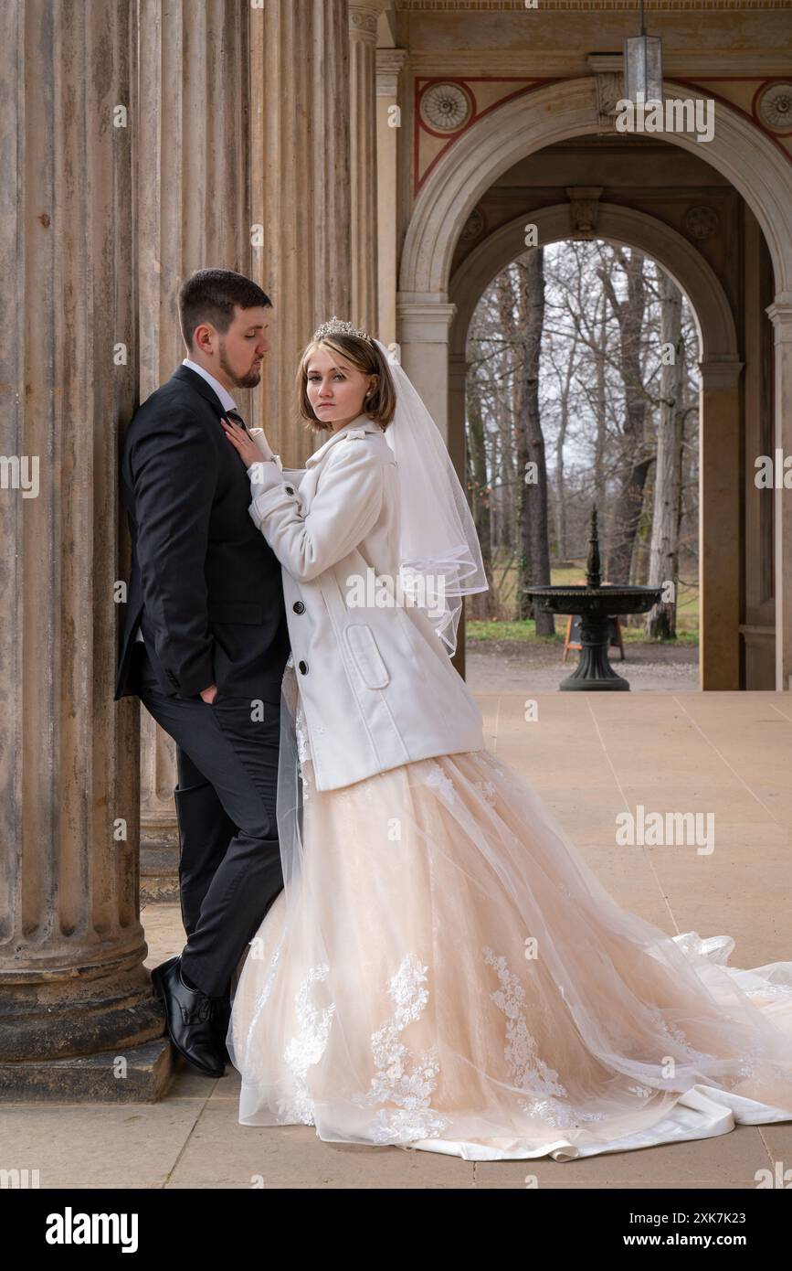 The bride and groom among the tall columns. The bride is wearing a long ...