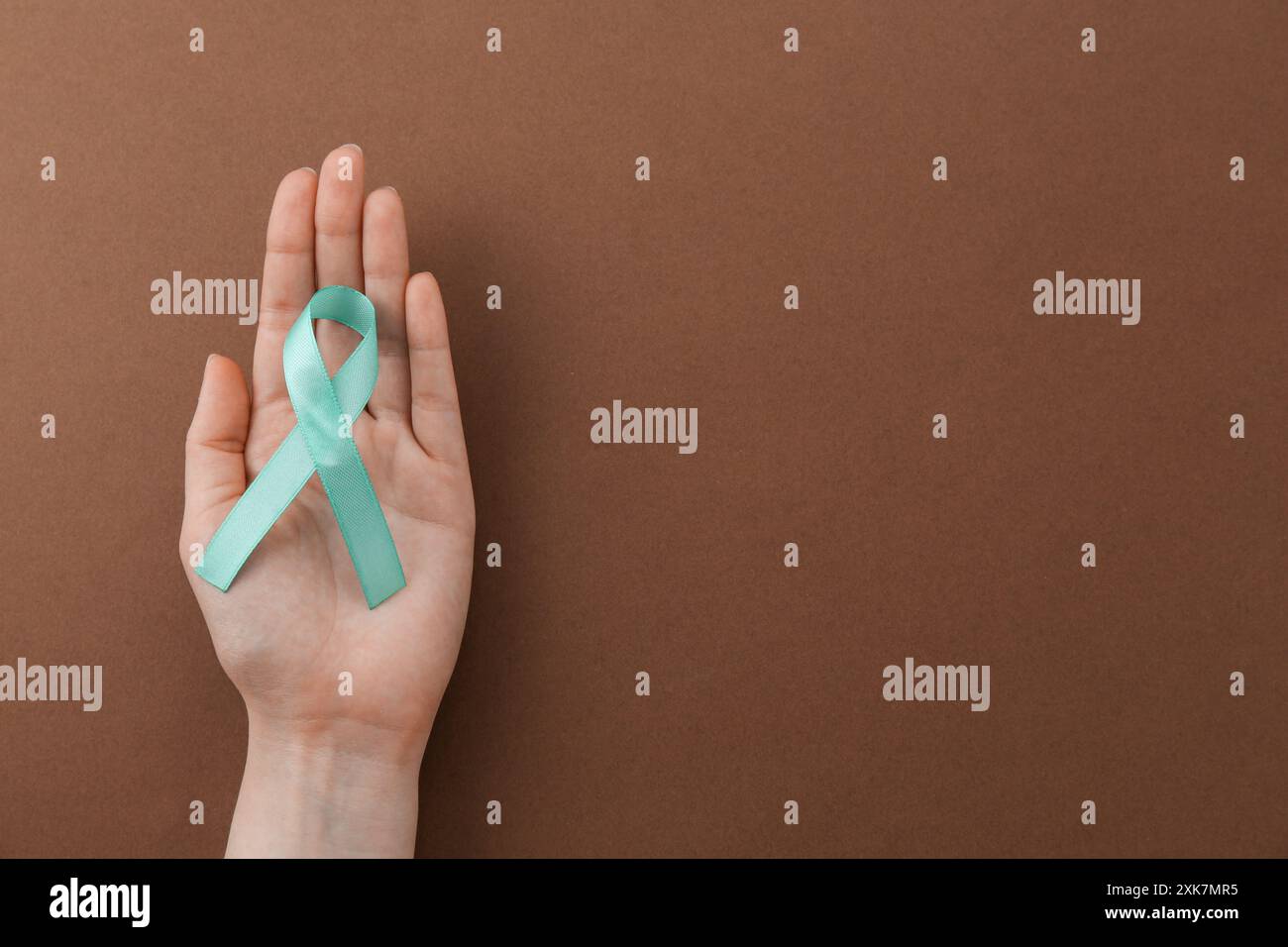Woman holding turquoise awareness ribbon on brown background, top view ...