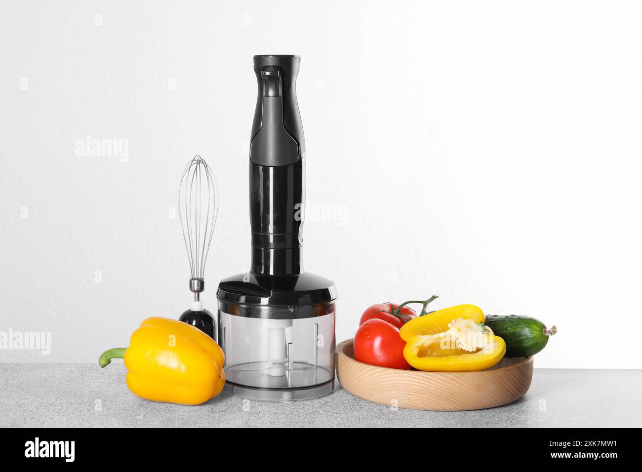 Hand blender kit and fresh vegetables on gray table against white ...