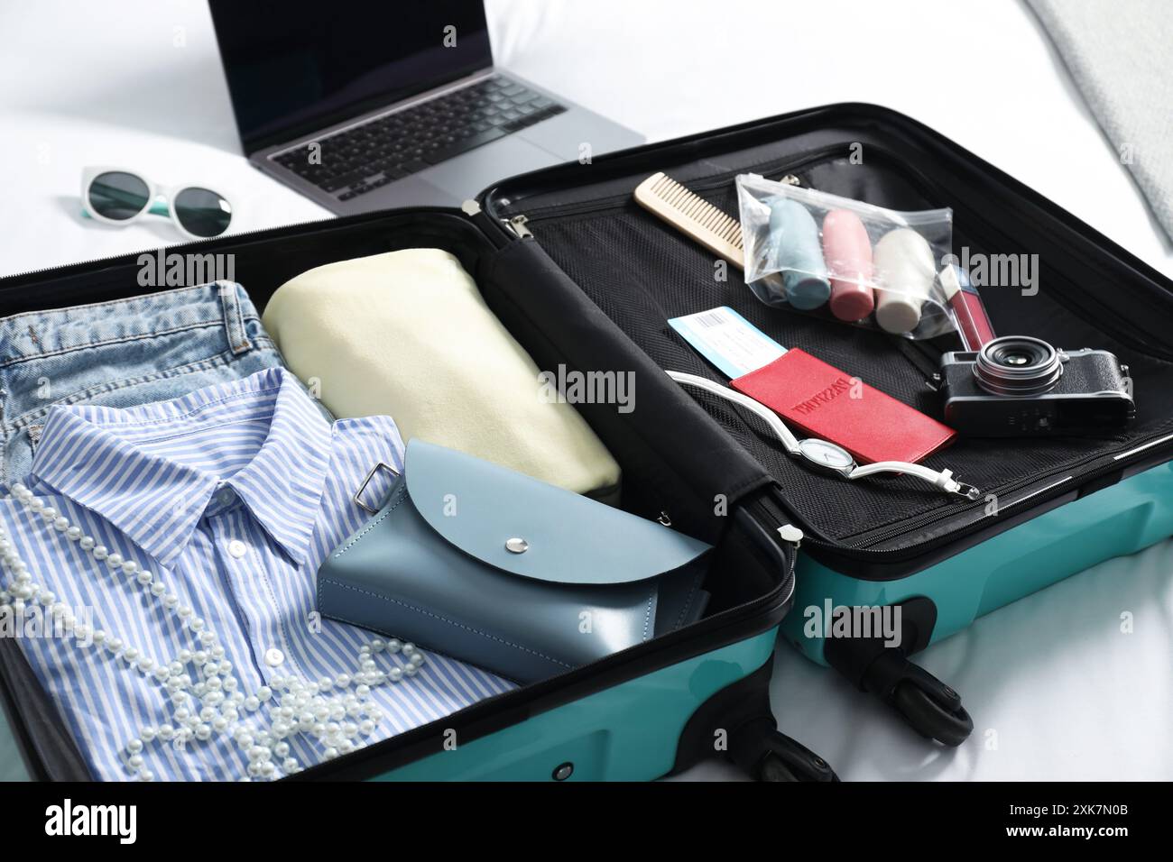Open suitcase with traveler's belongings on bed, closeup Stock Photo ...