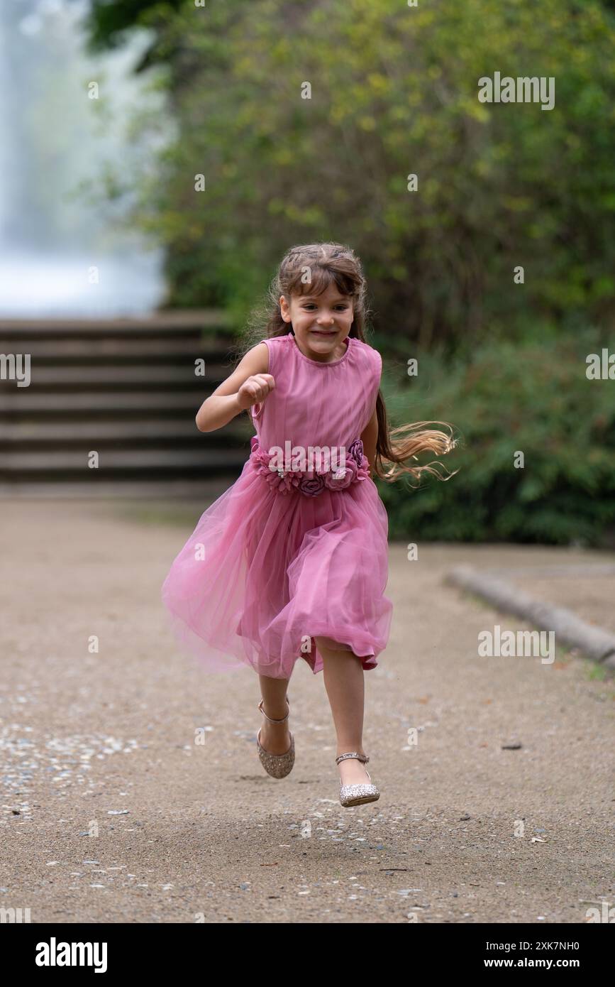 A little cute girl in a beautiful pink dress with long hair runs ...