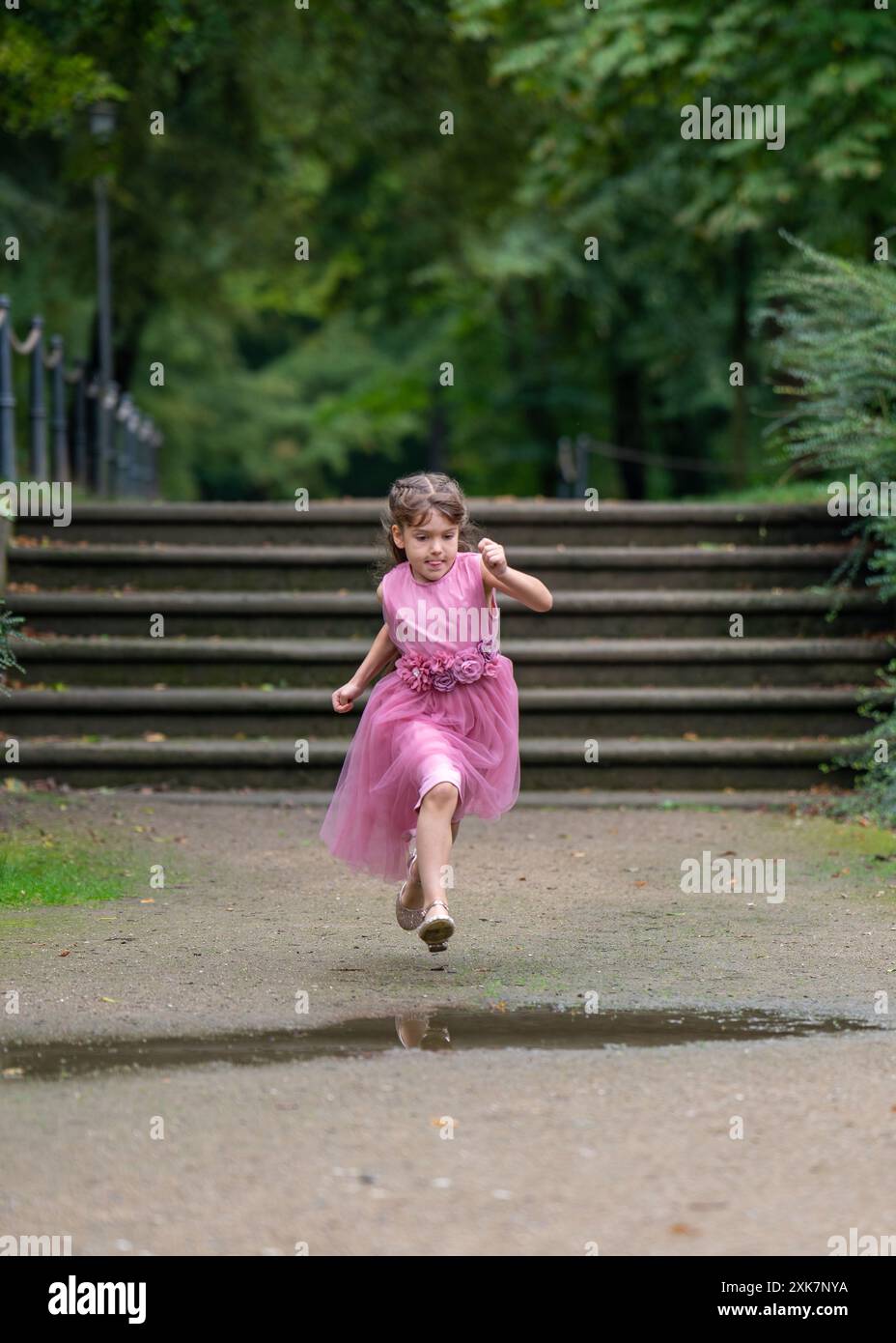 A little girl in a beautiful pink dress with long hair runs quickly and ...