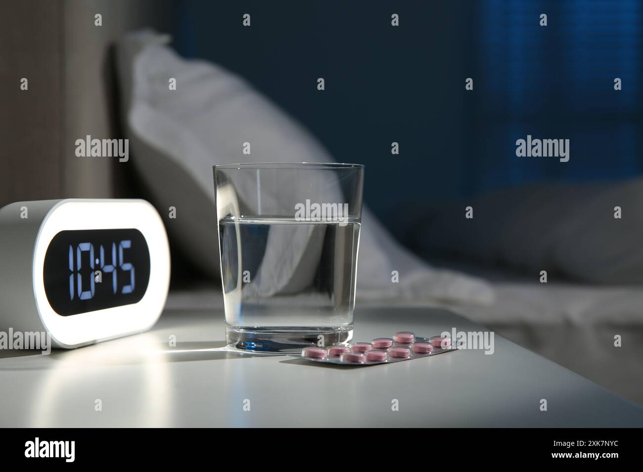 Insomnia treatment. Glass of water, pills and alarm clock on bedside ...