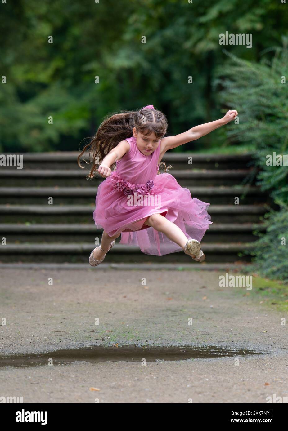 A little girl in a beautiful pink dress with long hair runs quickly and ...