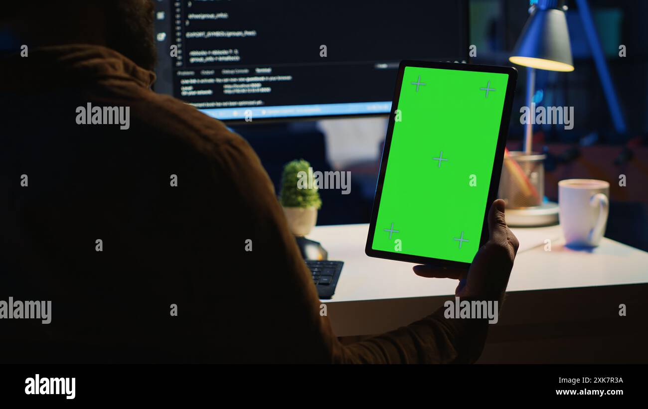 Software Developer Programming In Home Office Crosschecking Lines Of Code Between Green Screen