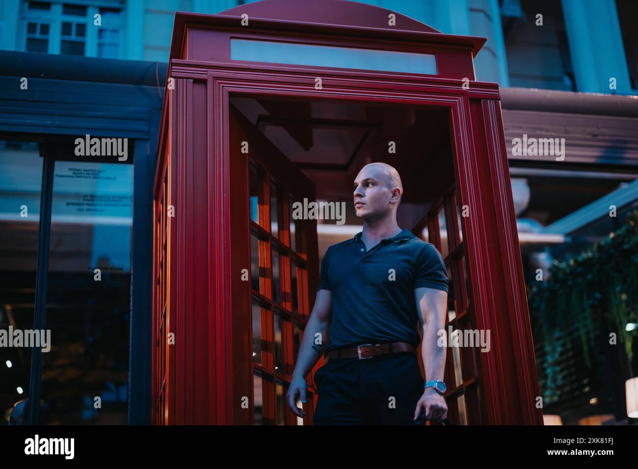 Man standing outside a red telephone booth at night in an urban setting ...