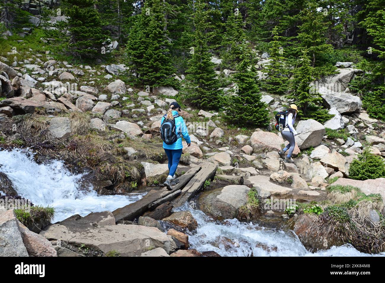 Two women hikers crossing stream on narrow log bridge on Lake Isabelle ...