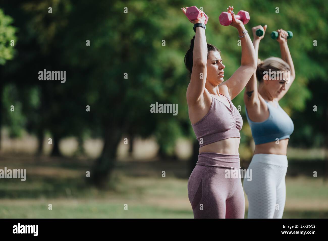 Two women doing outdoor workout with dumbbells in a park, focused on ...