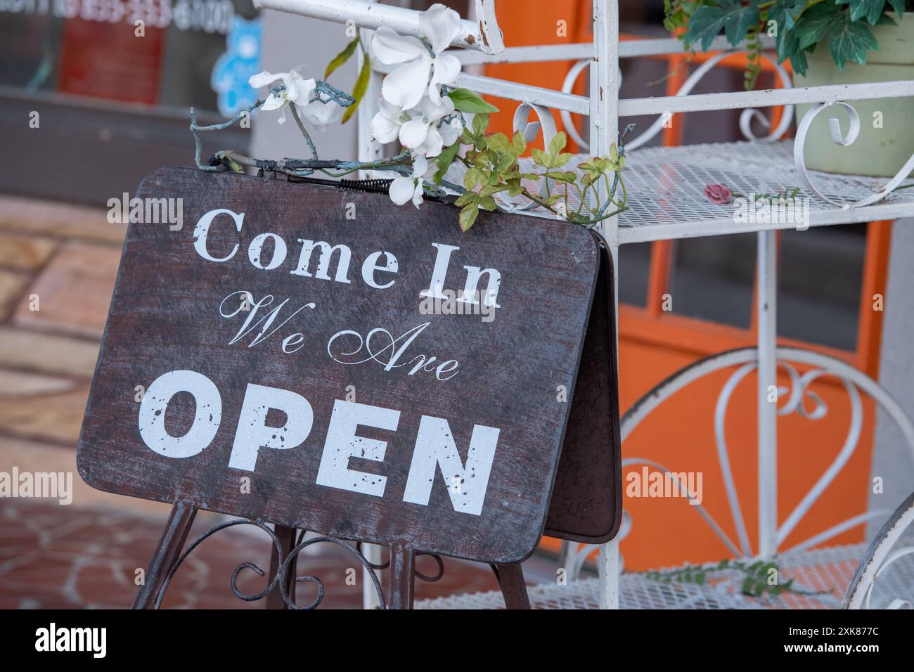A come in, we are open sign hanging from a white metal trolly on a ...