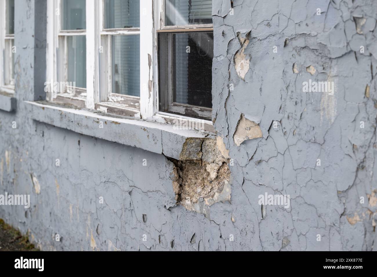 An old grey concrete building with peeling paint and a damaged window ...