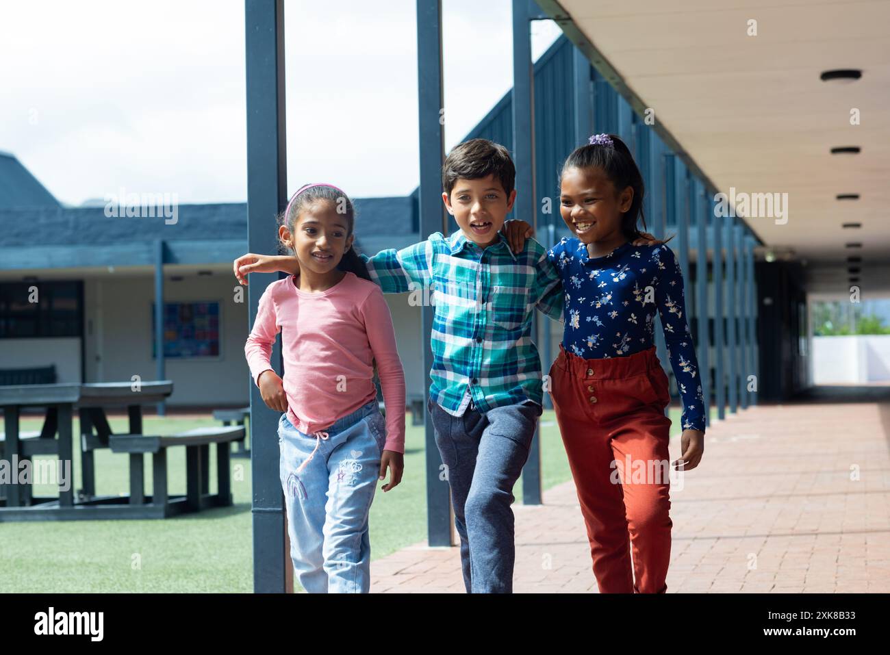 Three biracial children are walking together, smiling, in school Stock ...