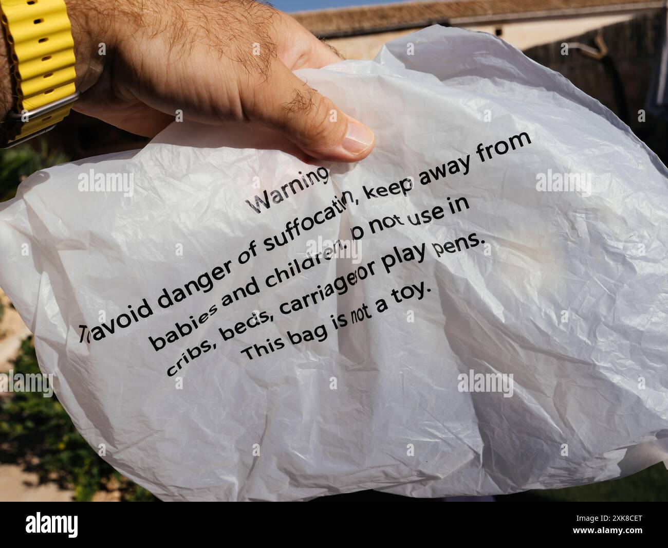 A close-up of a male hand holding a plastic bag with warning text to ...