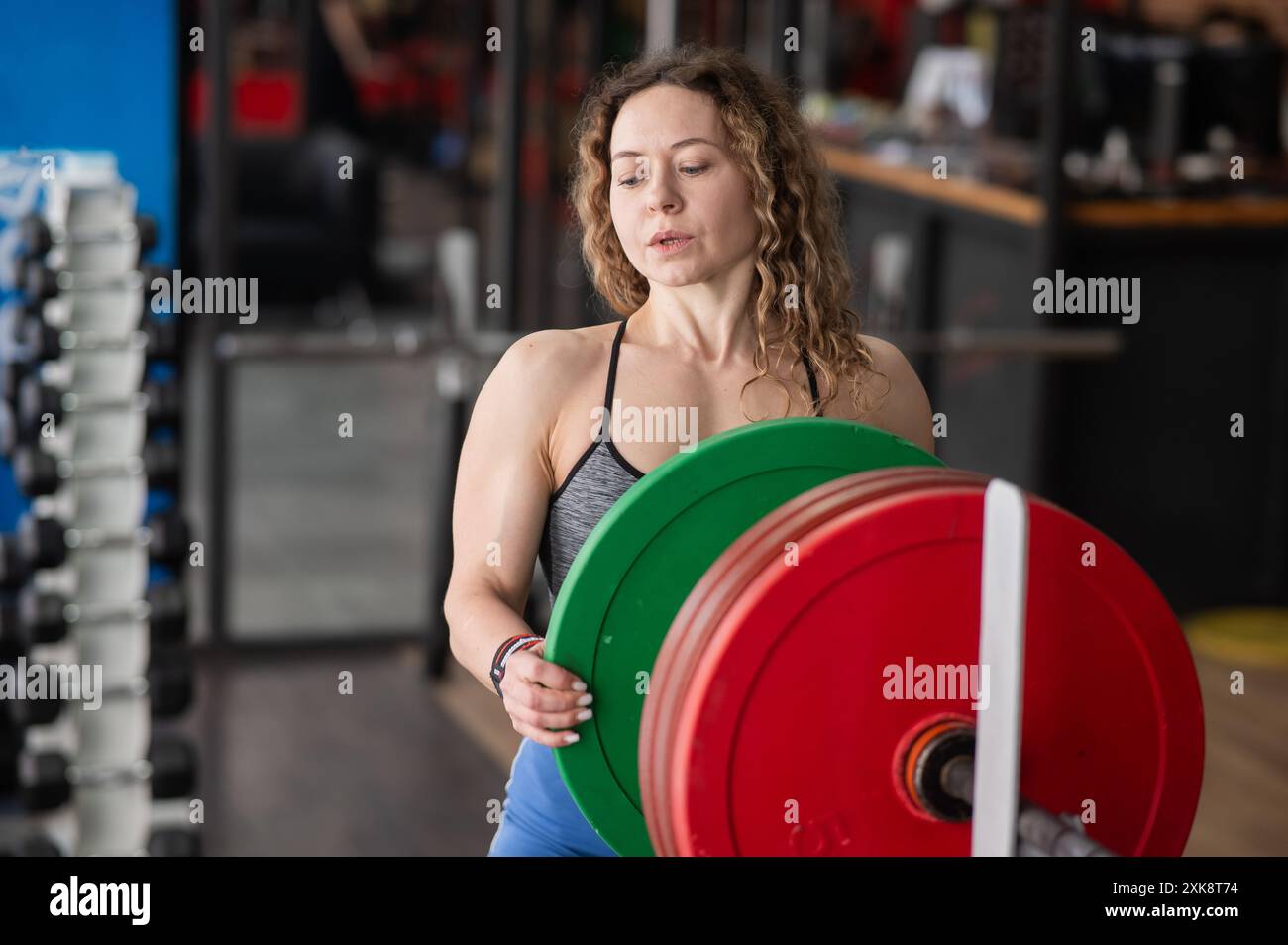 Caucasian forty year old woman putting a weight plate on a barbell in ...