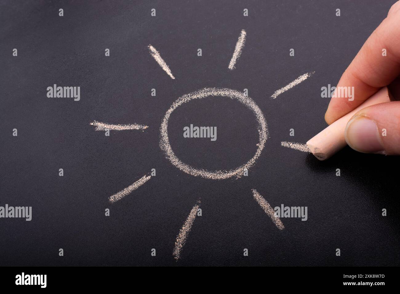 Hand drawing sun by chalk with light ray shape on blackboard background ...