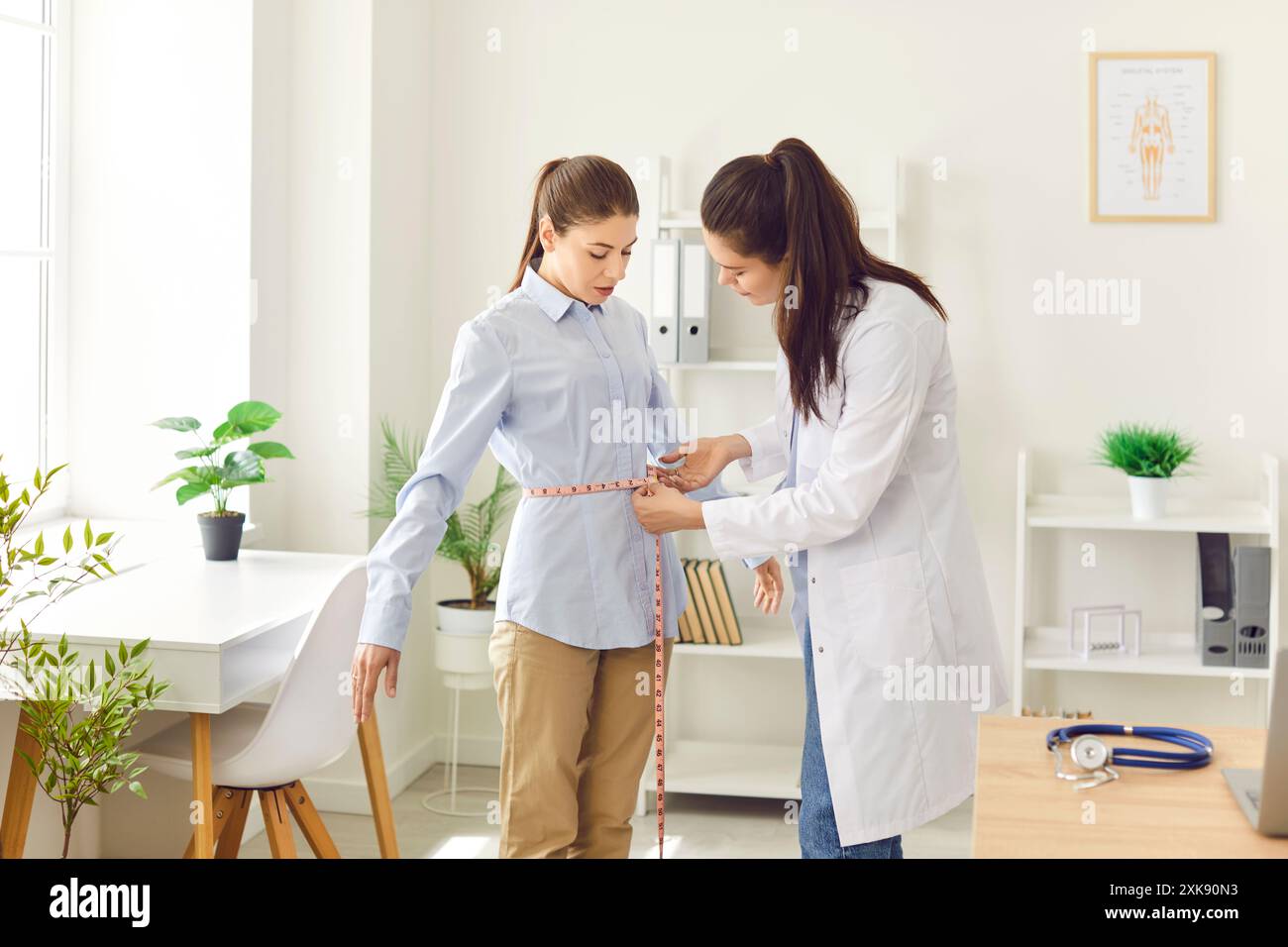 Doctor, nurse measuring young female patient waist line with tape ...