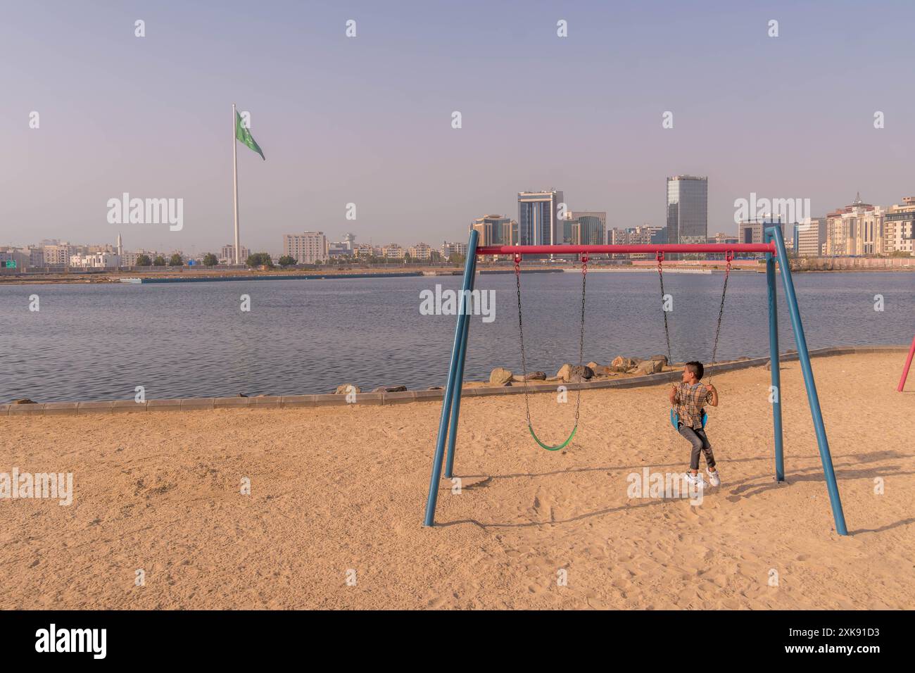 The Arabian boy on swings on the coast of Jeddah harbor with the city ...