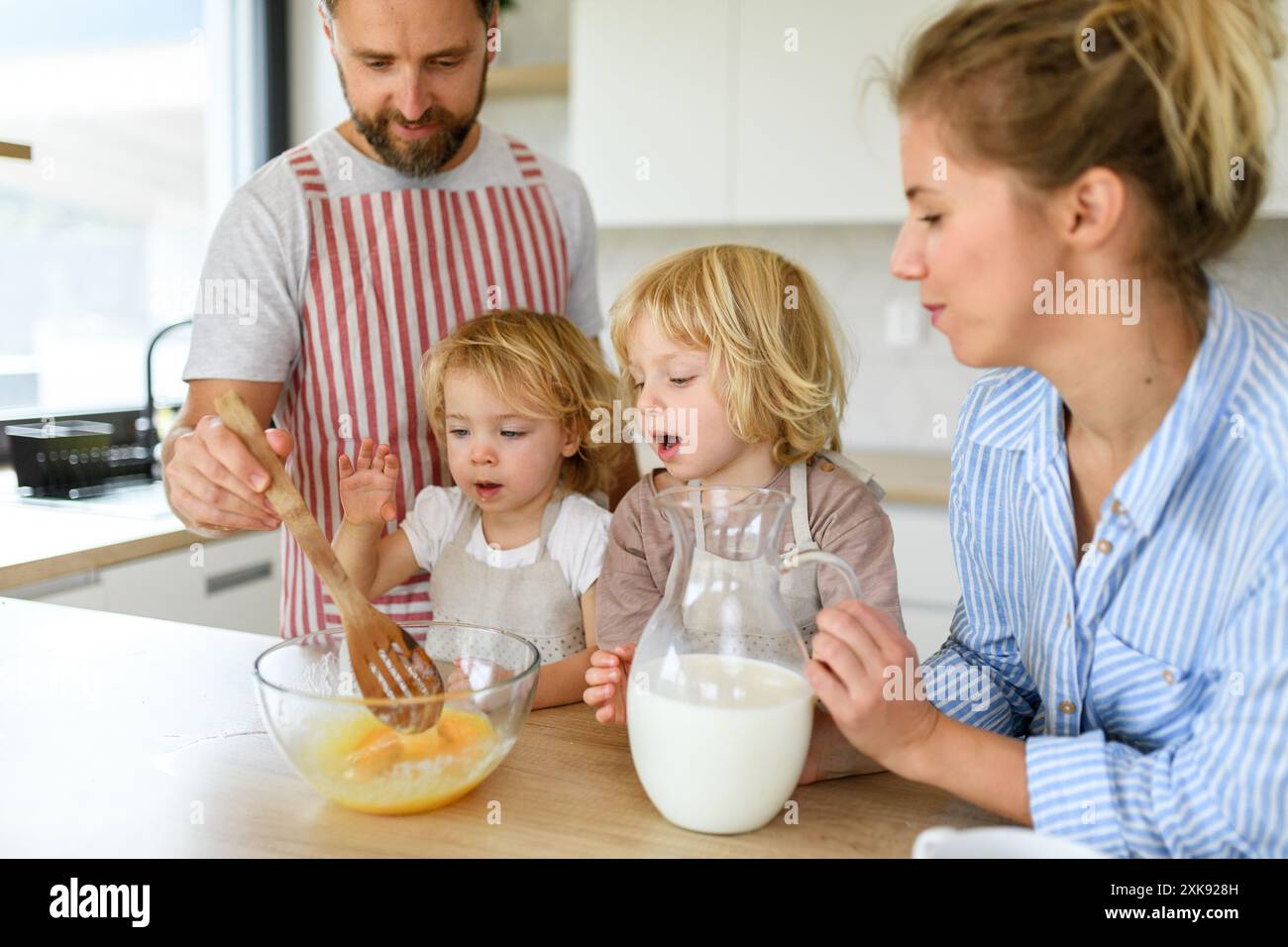 Young nuclear family making pancakes together. Parents and children in ...