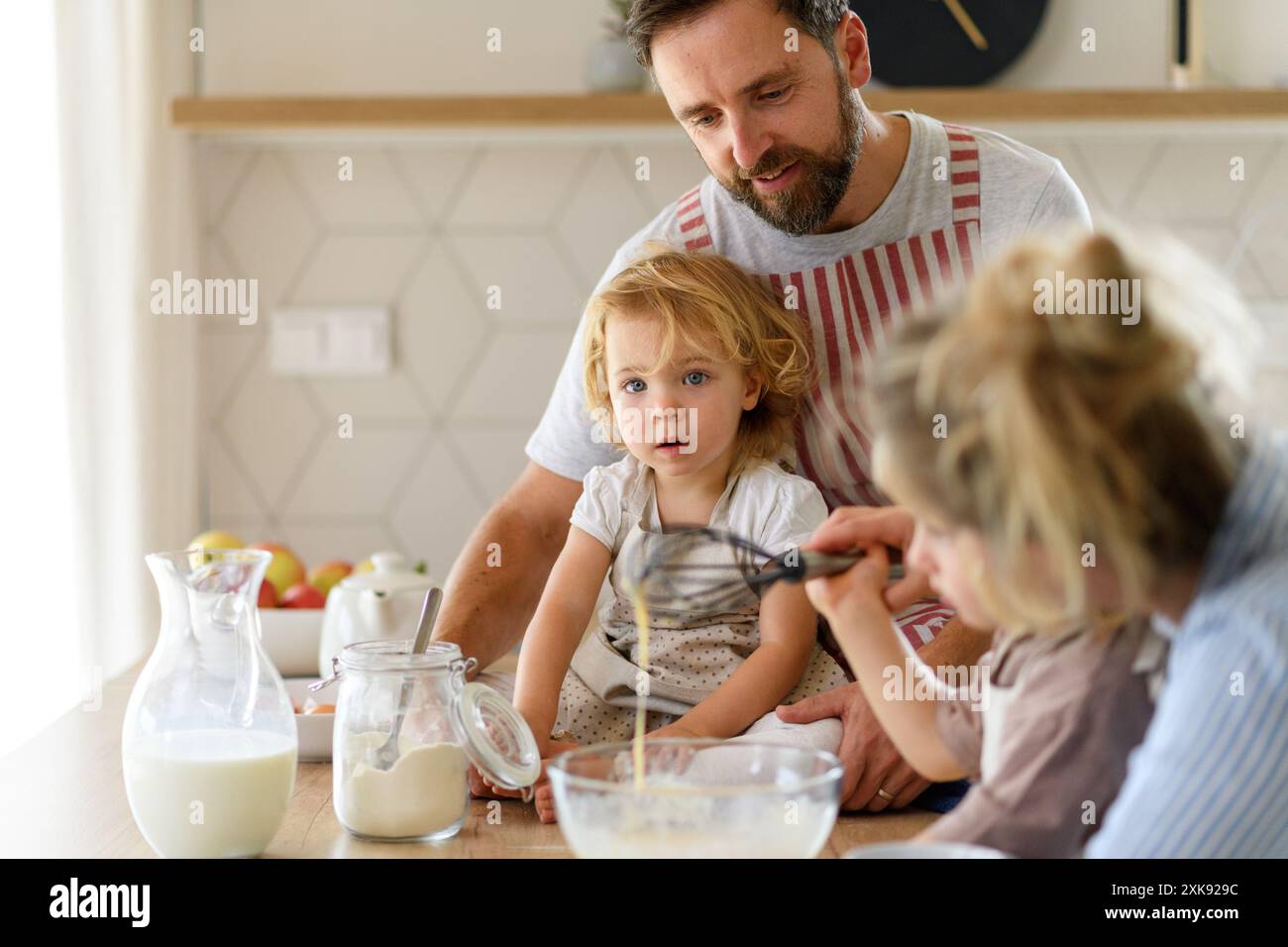 Young nuclear family making pancakes together. Parents and children in ...