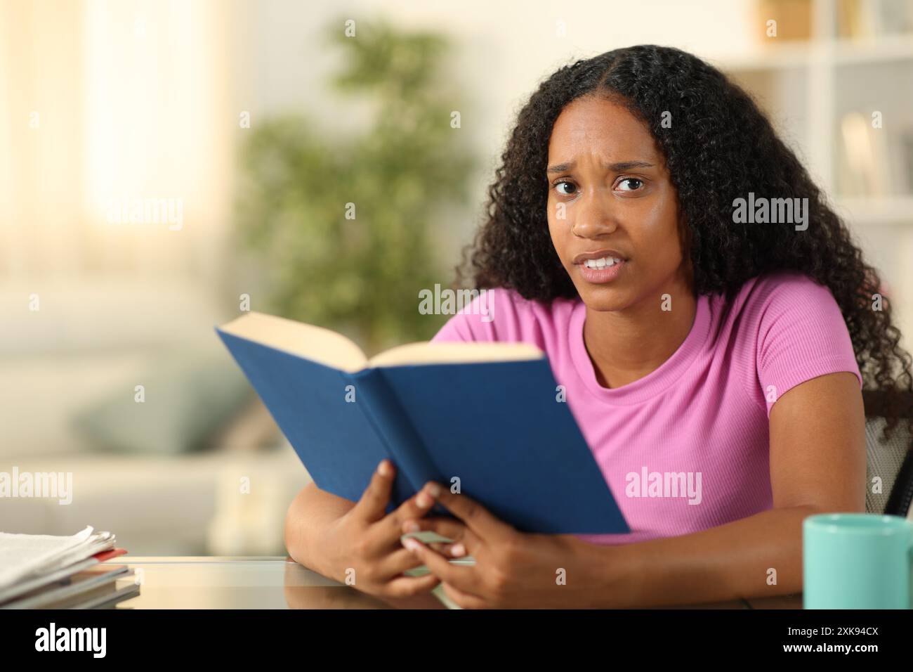Disappoited black woman reading a paper book looks at you at home Stock ...