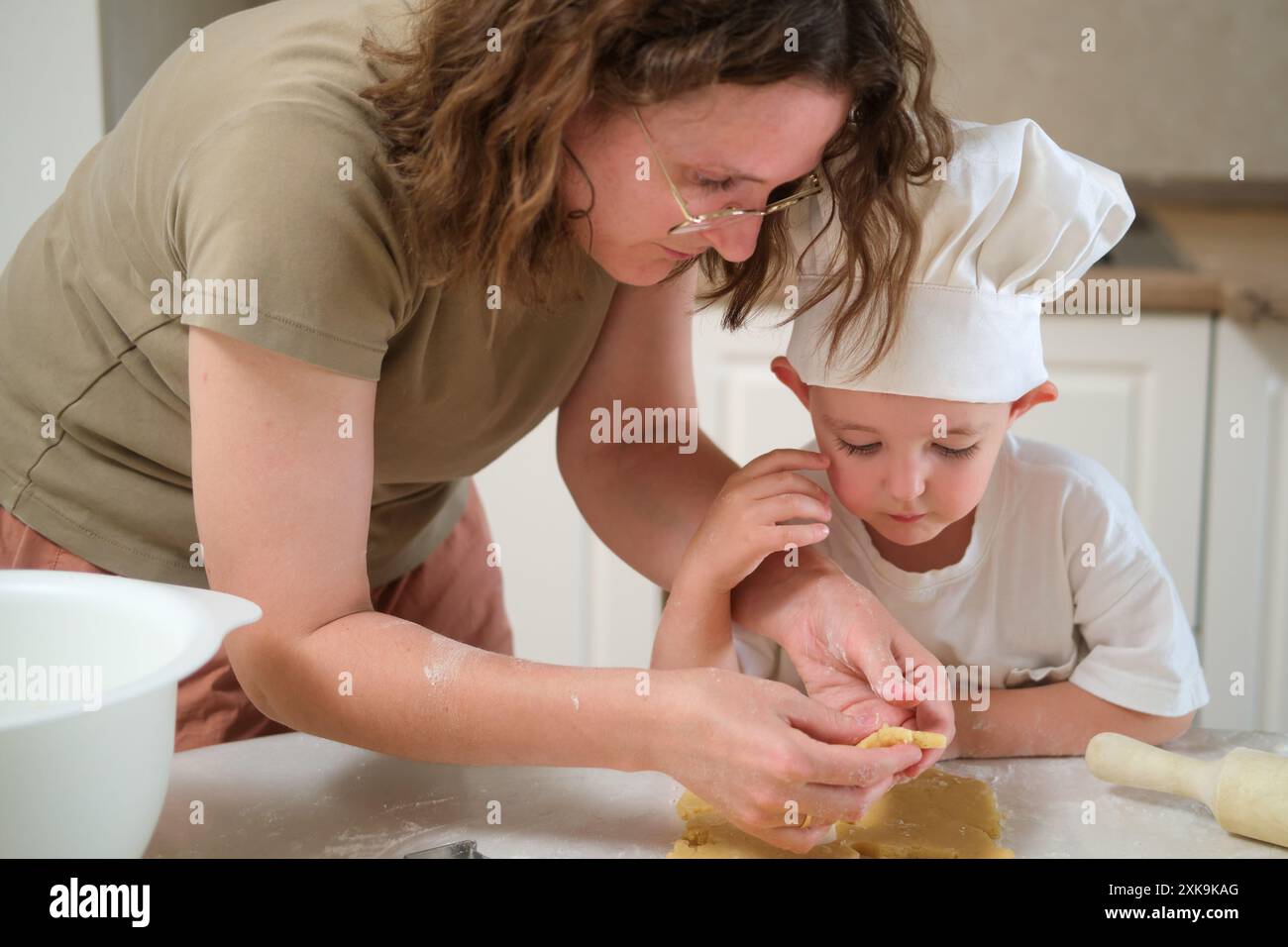 A woman is teaching a child how to make a pastry. The child is wearing ...