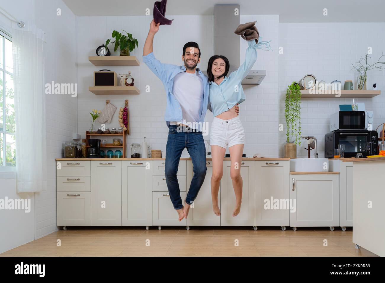 Cheerful young european lady and male washing dishes in modern kitchen ...