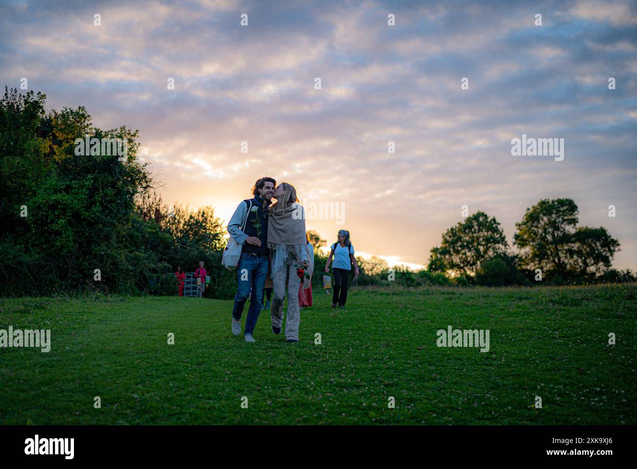 A couple kiss as they make their way through a field at sunset on the ...