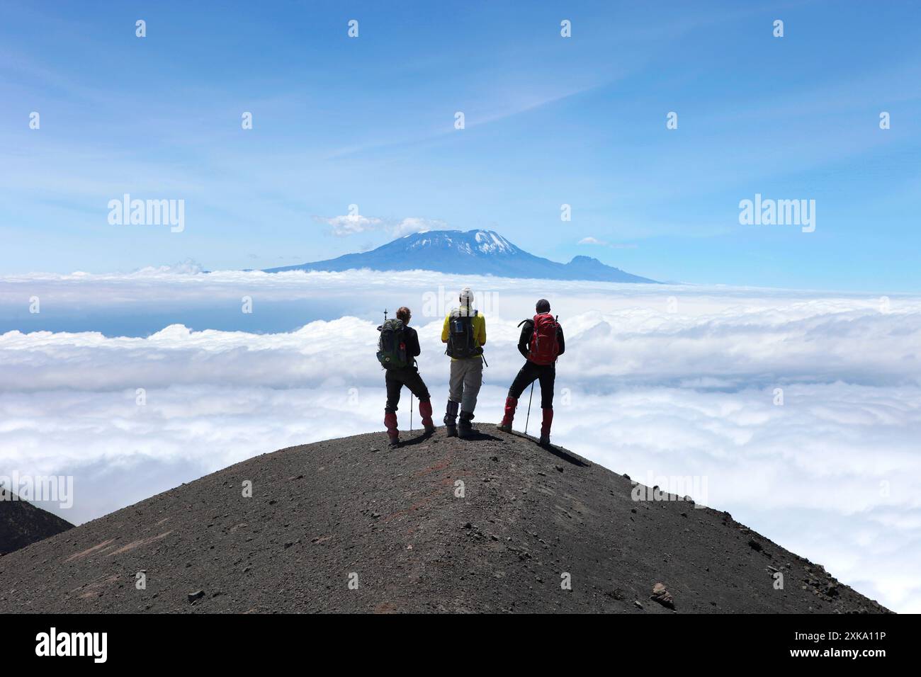 Three hikers are looking at Mount Kilimanjaro from the rocky ridge of ...